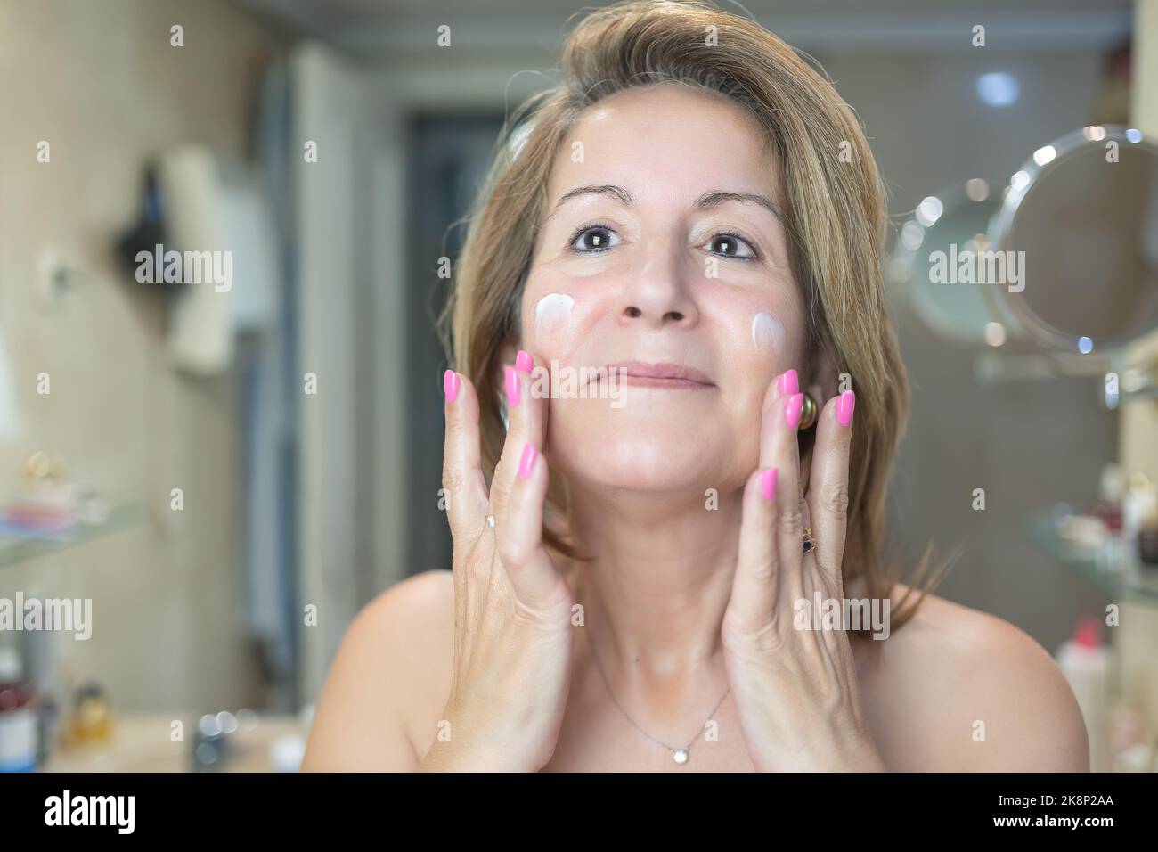 Mature white woman with cream on her face for skin care and in front of ...