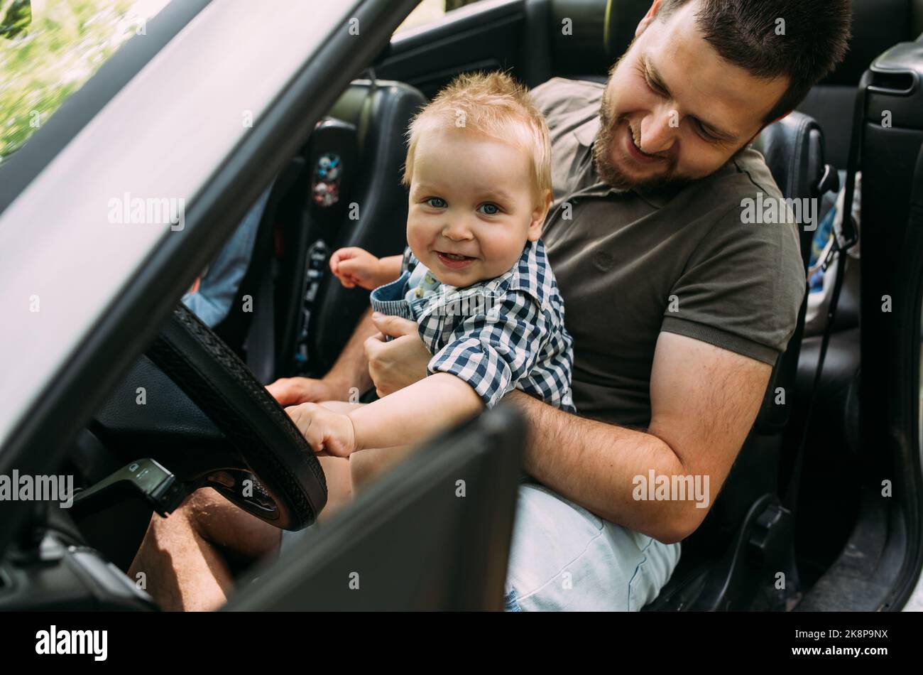 Dad shows his little son how to drive car while sitting behind wheel ...