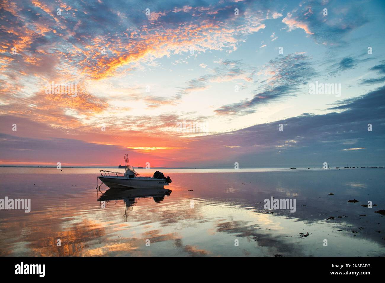A scenic view of a lonely motorboat on the reflective sea at sunset ...