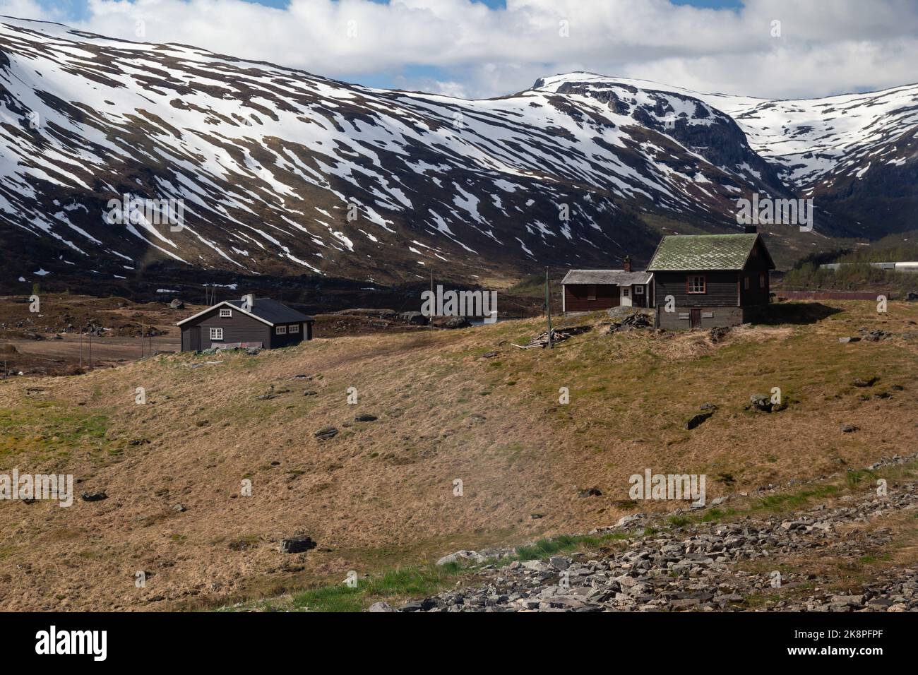 A beautiful shot of wooden houses on a rural field near snowy mountains ...