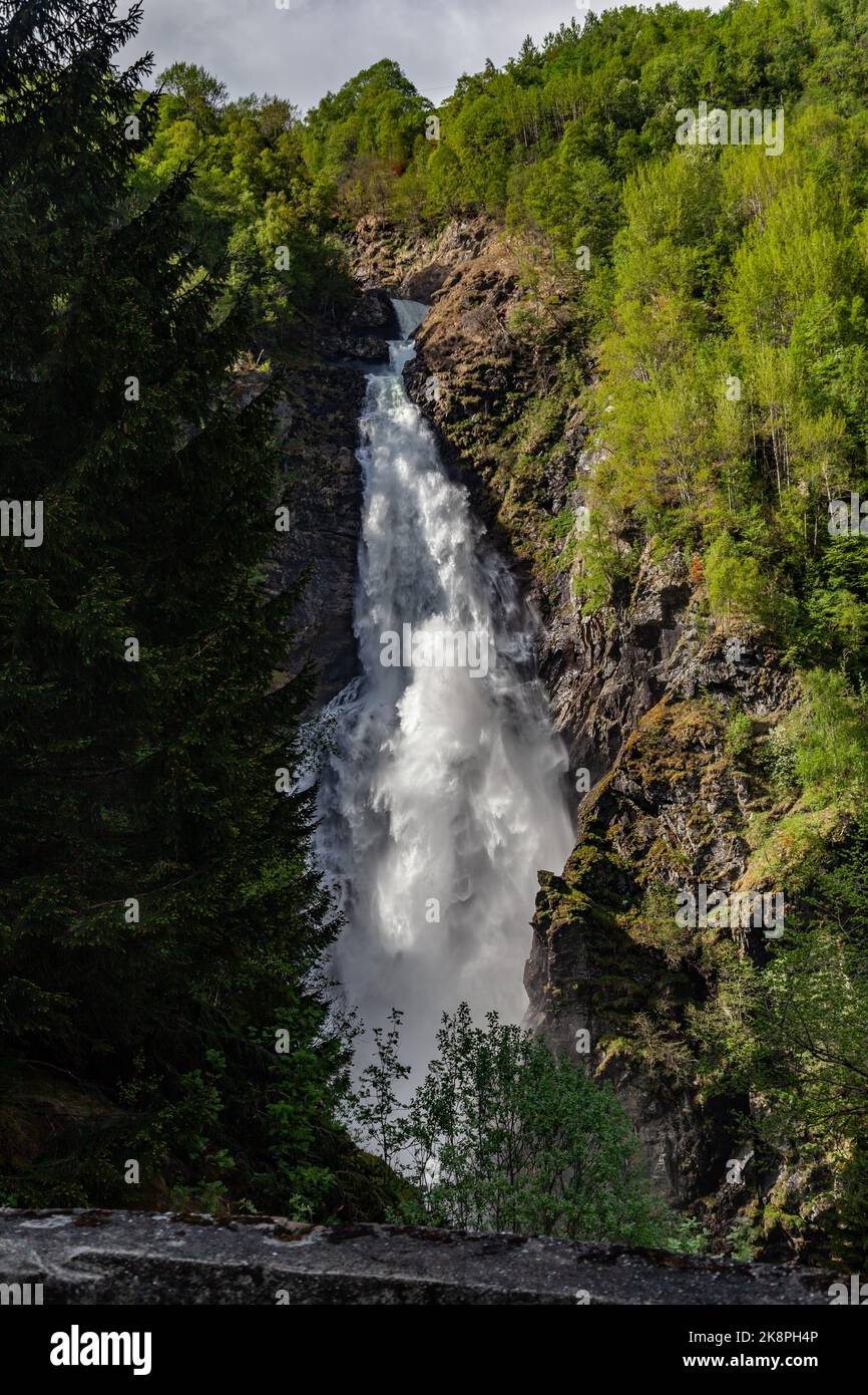 A vertical shot of a flowing waterfall on the side of a rocky mountain ...