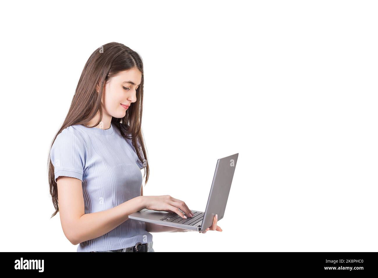Side view of a young woman holding a laptop in her hand, typing a ...
