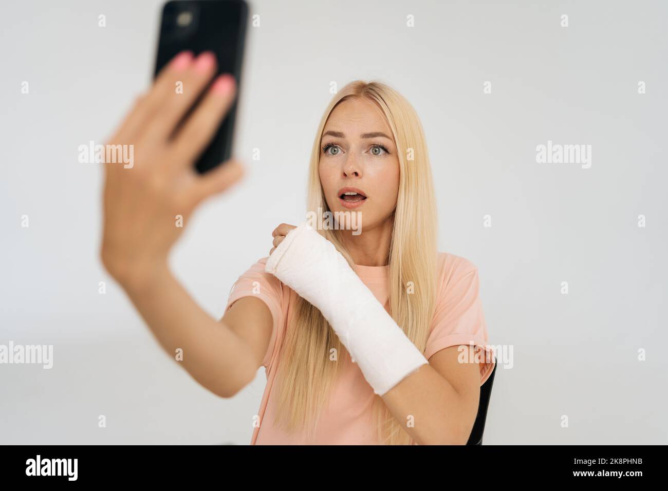 Portrait of shocked young blonde woman with broken arm wrapped in ...