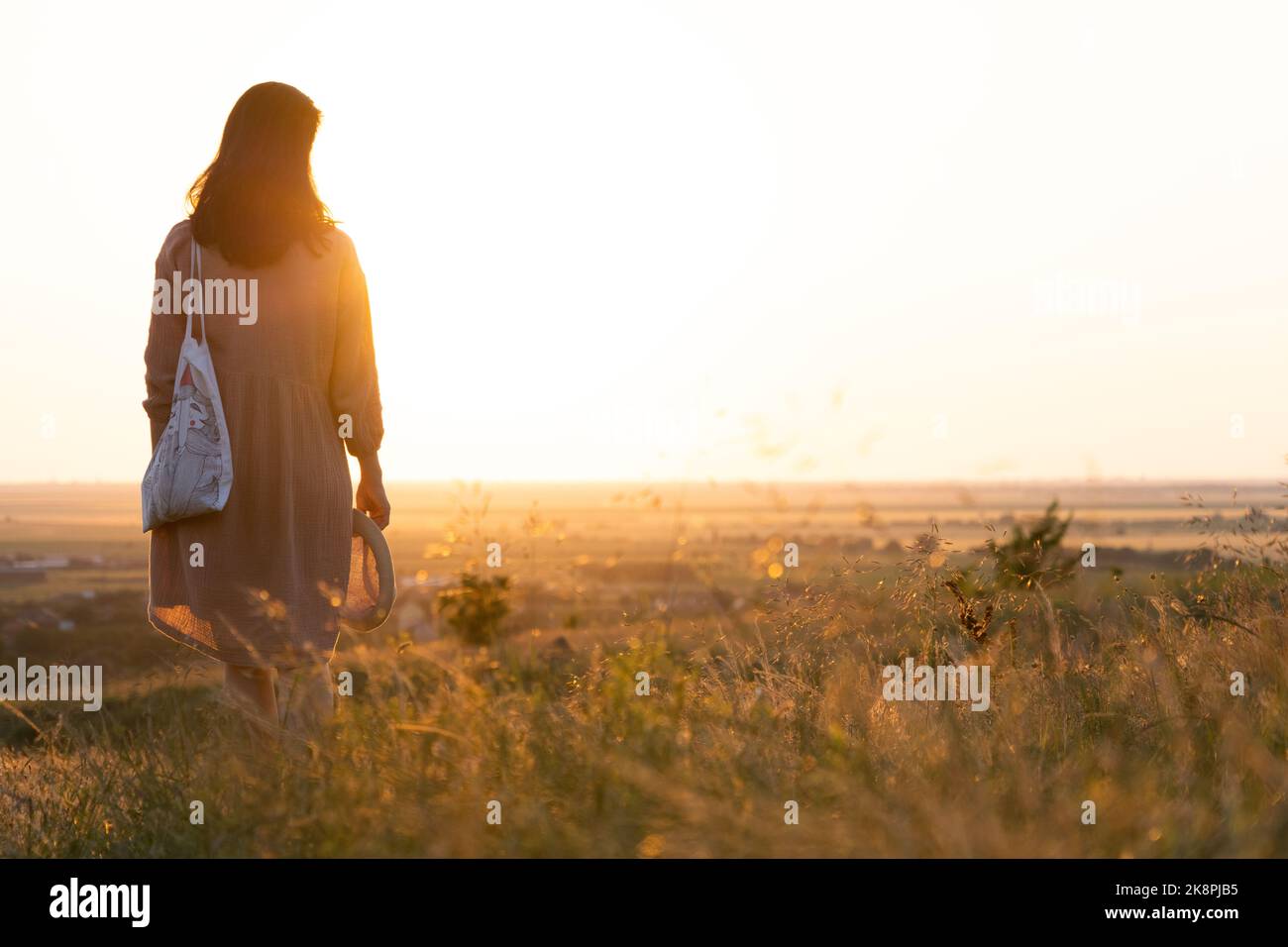 a back view of a cute girl with a dress and bag in a field during ...