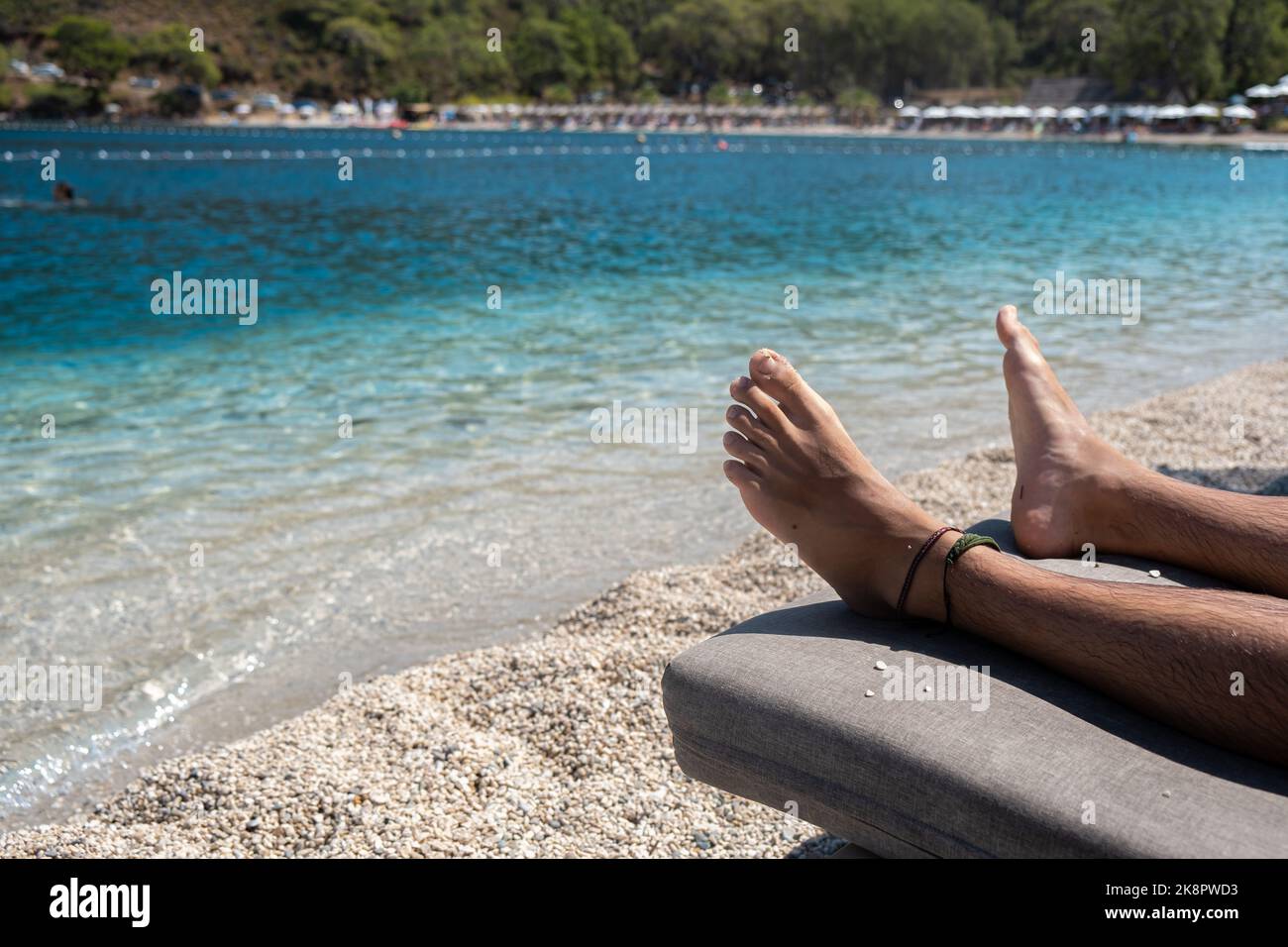 man tourist legs on sun-bed at tropical beach resort white sand and ...