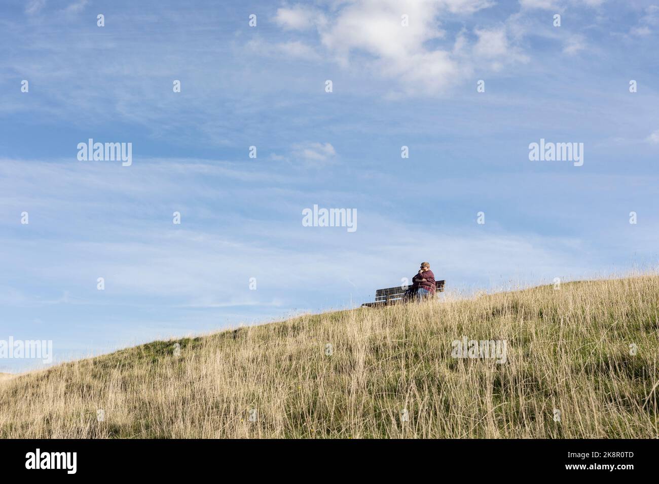 woman sitting alone on a bench deep in thought under blue summer skys ...