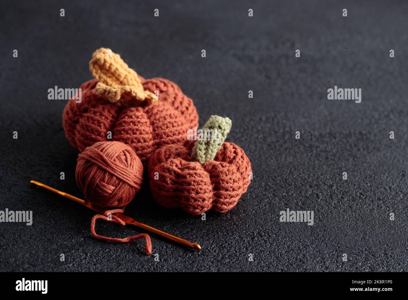Cute crochet knitted orange pumpkins on black background with a ball of ...