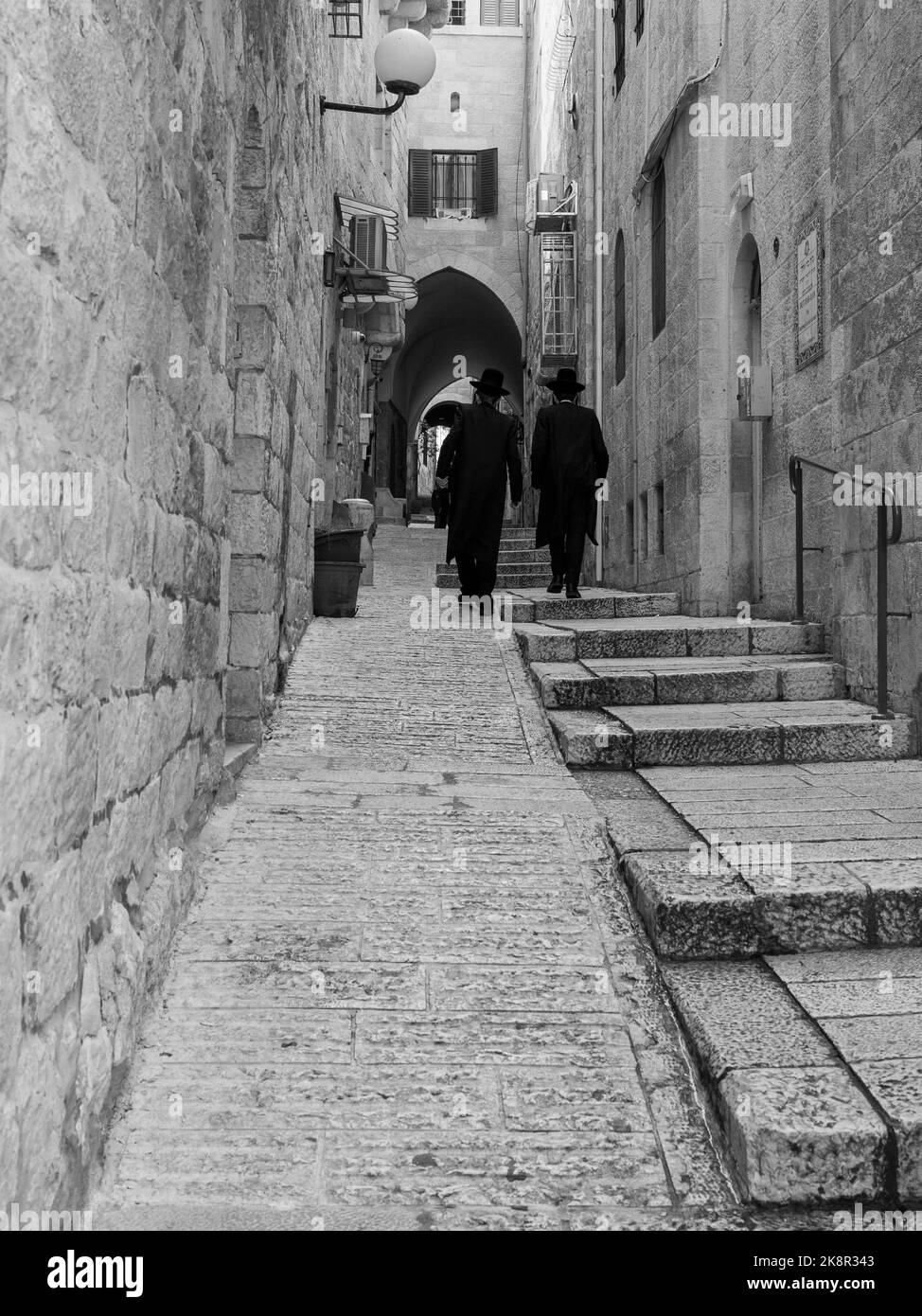 A grayscale shot of two Jewish men walking by the narrow streets of the ...