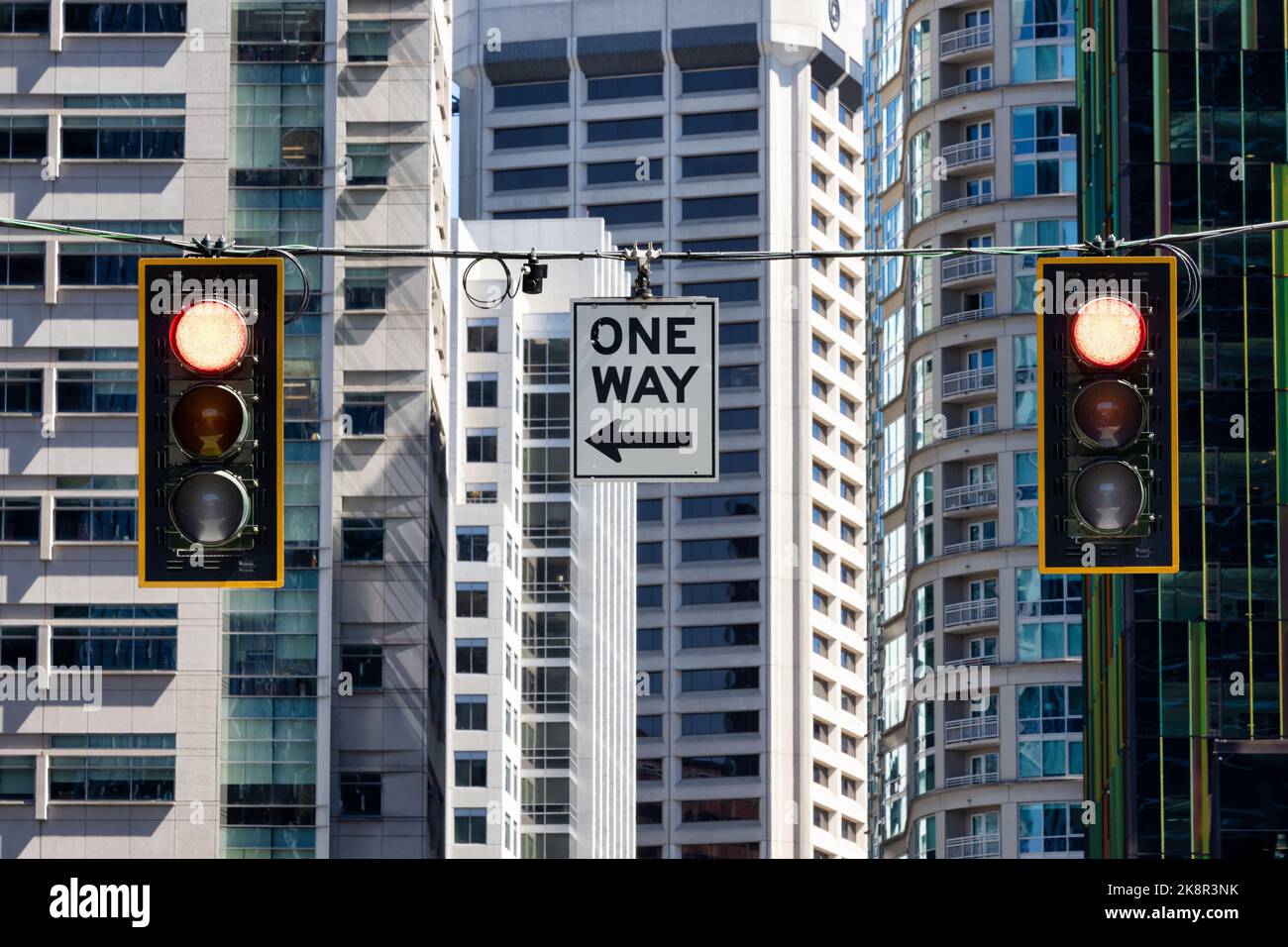 A one way sign hanging between two traffic lights on high buildings ...