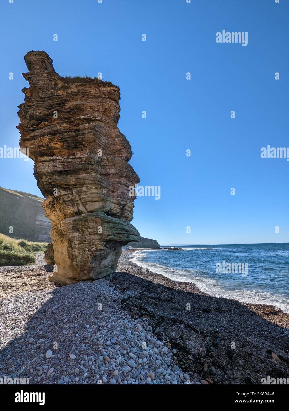 A vertical shot of a tall rock formation on the shore with the sea and ...