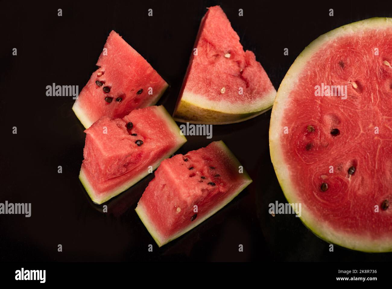 A top view of watermelon slices and halved watermelon on black surface ...