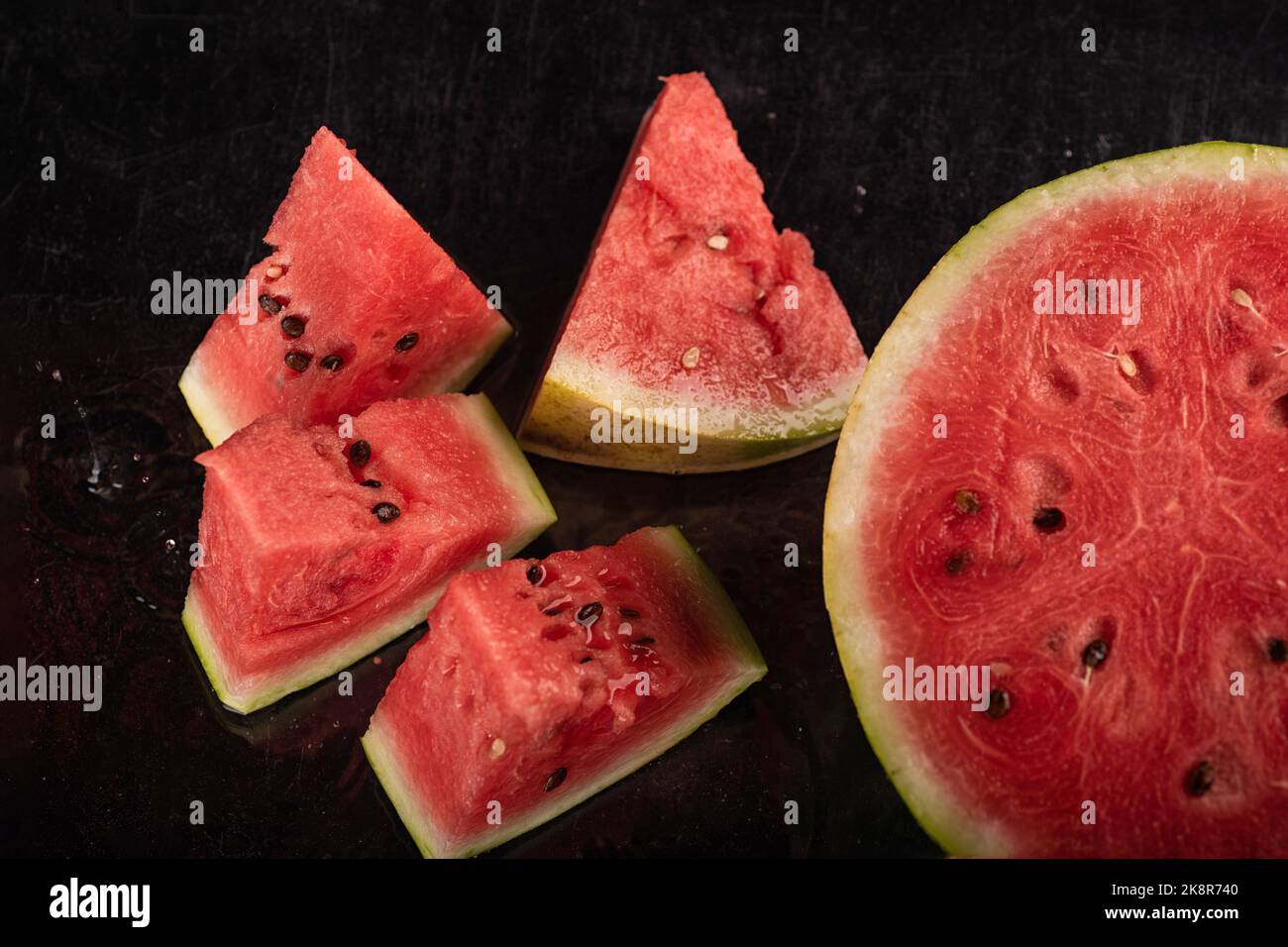 A top view of watermelon slices and halved watermelon on black surface ...