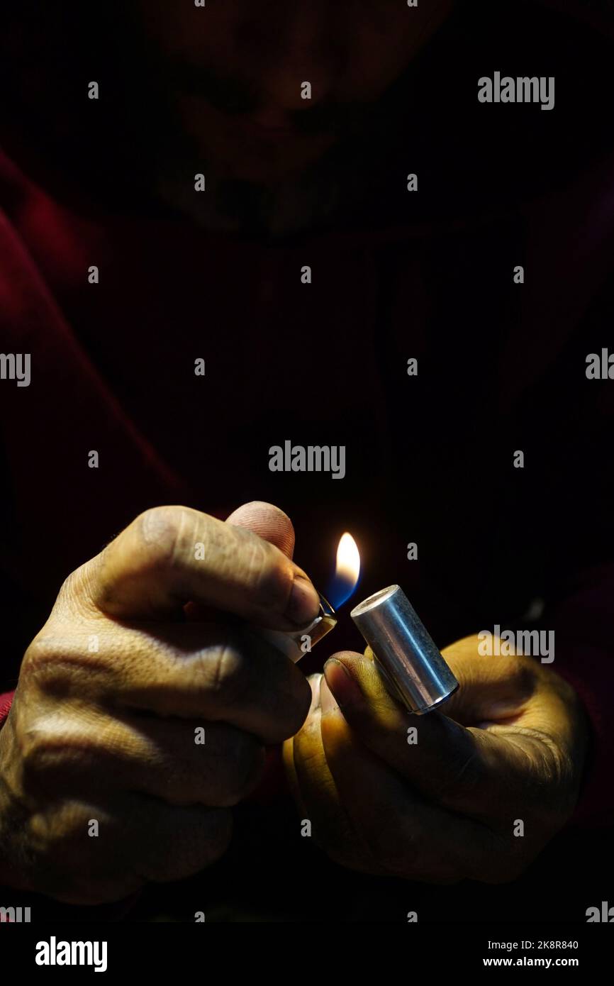 A closeup of a man in a red hoody lighting the drug with a metal pipe ...