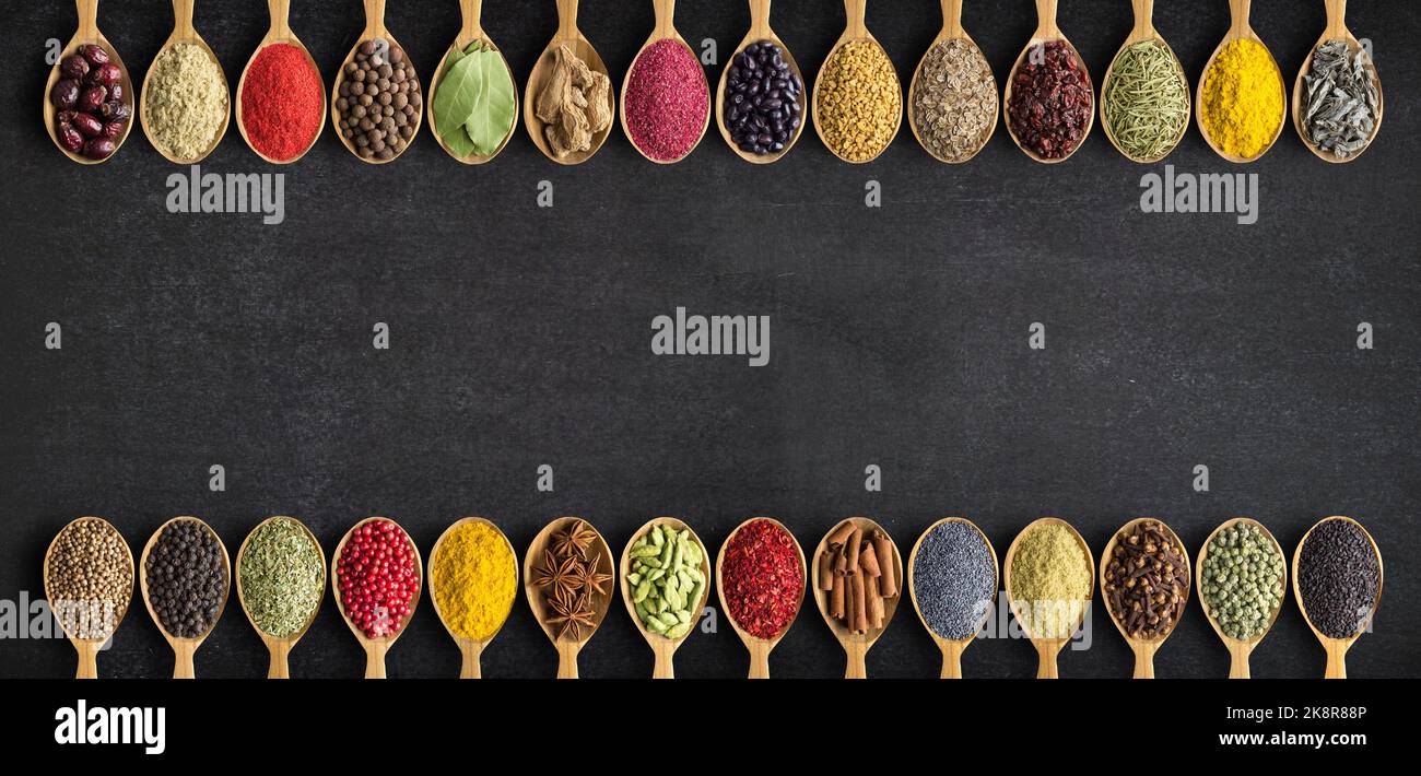 spices in wooden spoons on black table. set of condiments and herbs ...