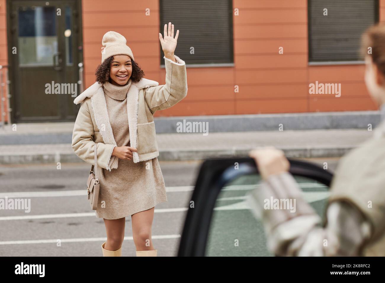 Girl in warm clothing waving her friend while they meeting outside ...