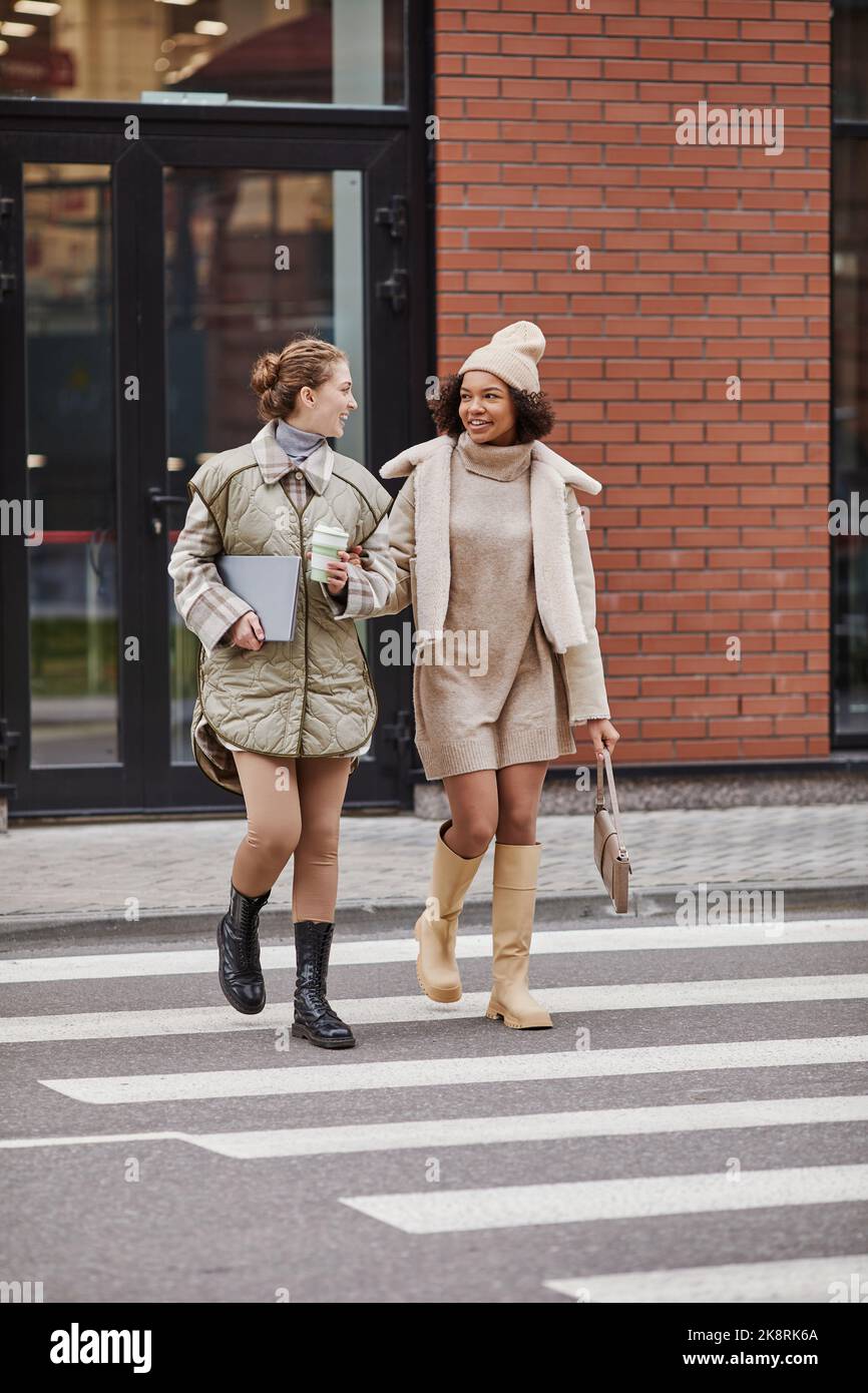 Two young friends crossing the road and talking, they going together to ...