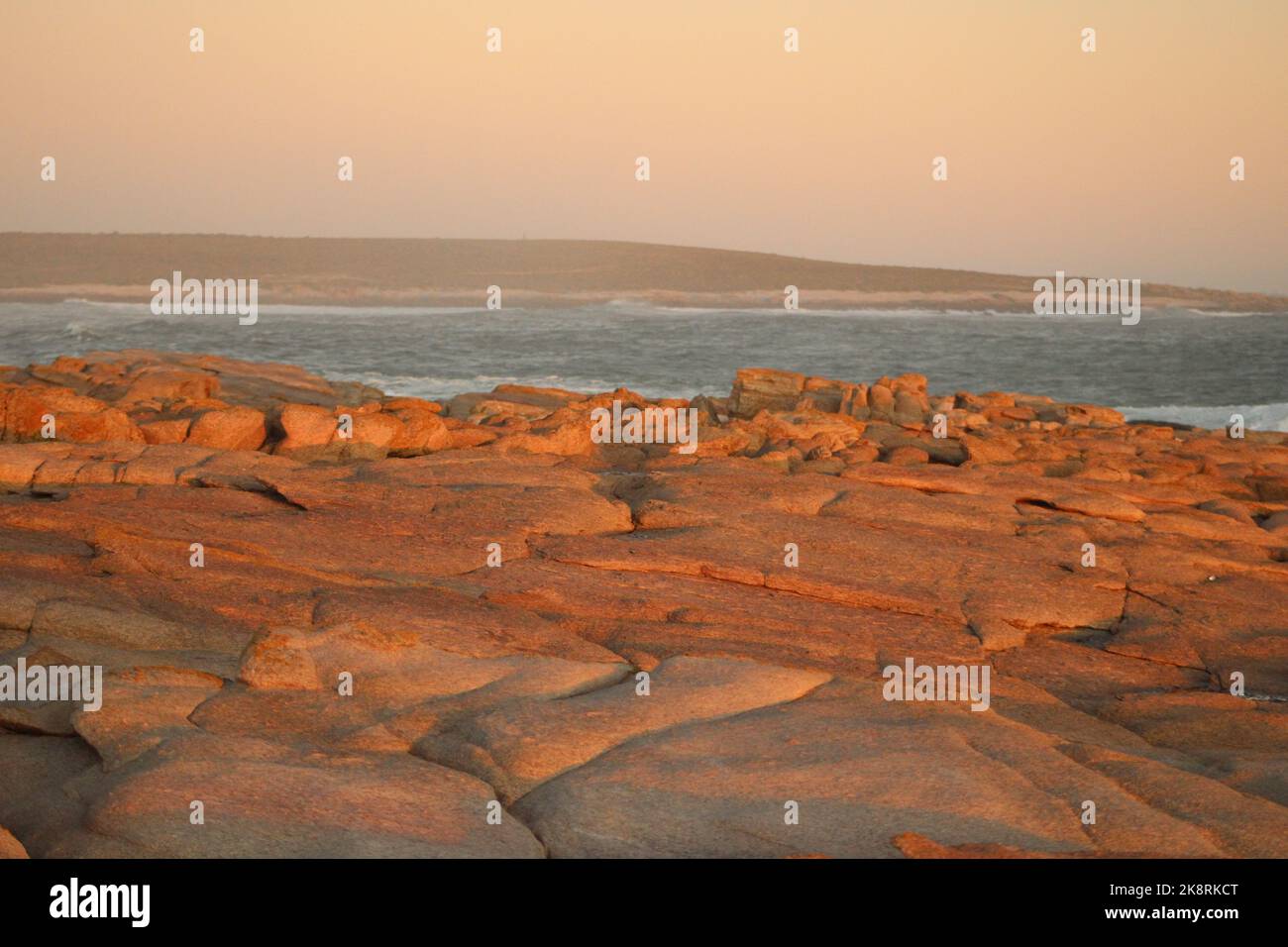 A scenic view of a rocky shore of a beach with a small hill on the ...