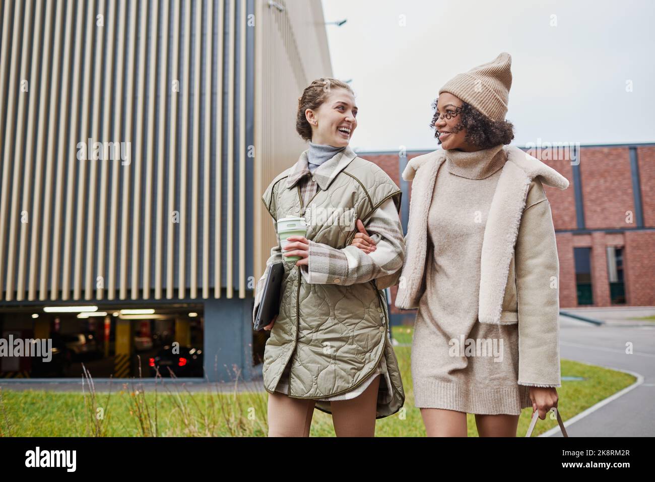Two young friends smiling and talking while going by foot together for ...