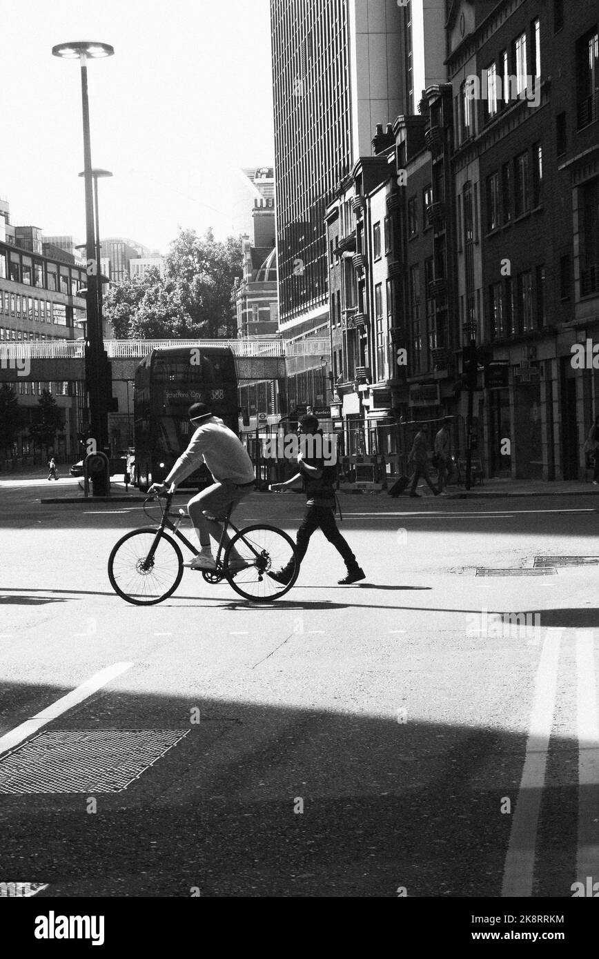 A greyscale shot of two men, one on the bike, crossing the street Stock ...