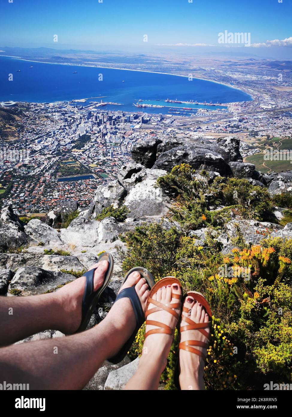 A vertical view of pairs of feet hanging over a cliff on Table Mountain ...