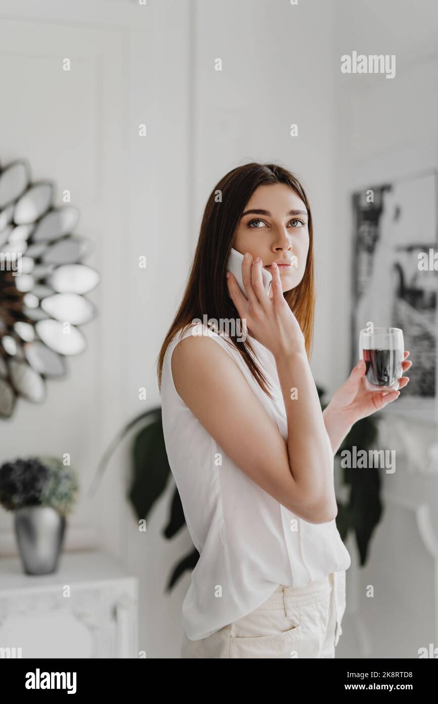 Young businesswoman talking on the phone and holding glass with coffee ...