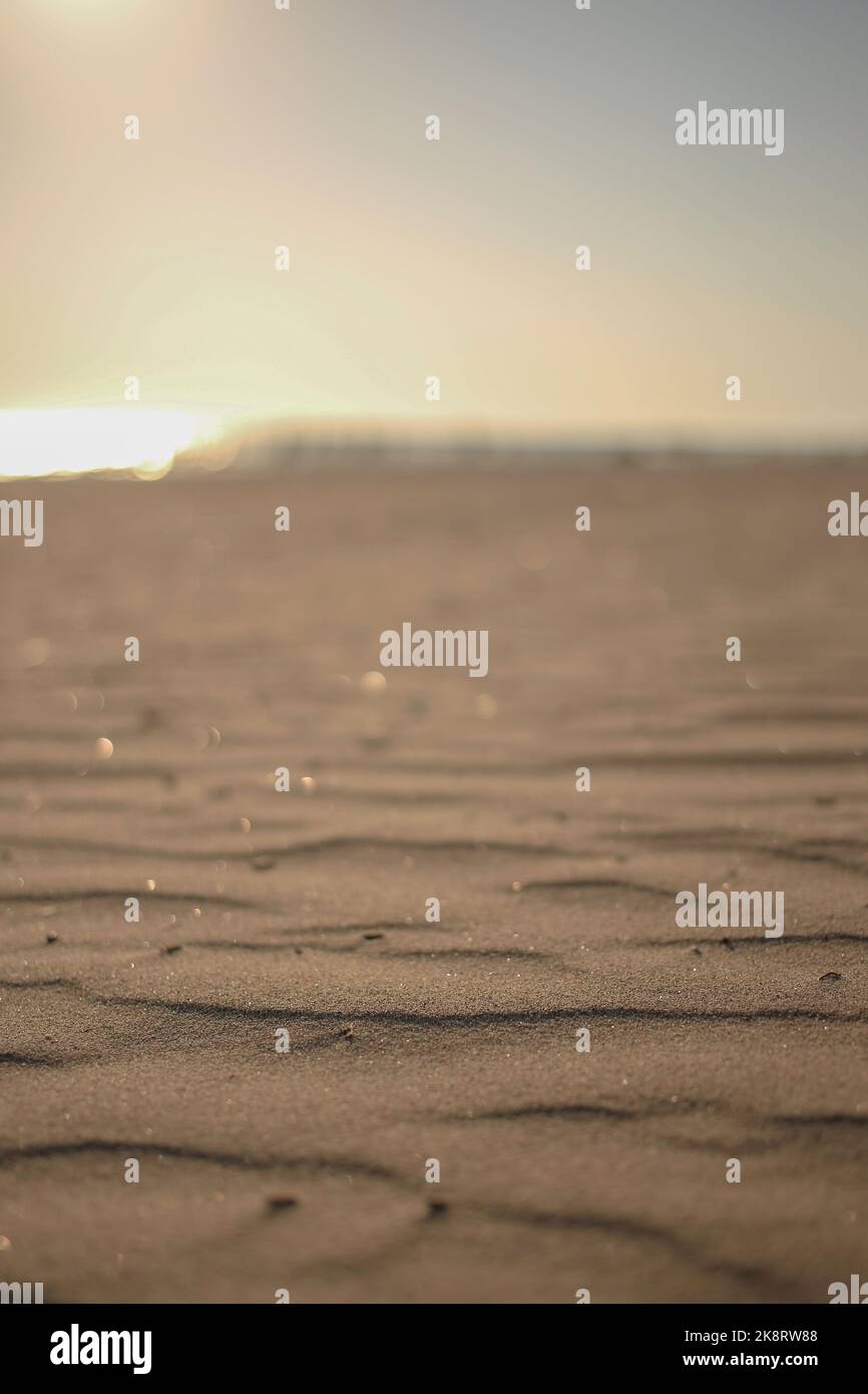 A vertical shot of wet sand with wavy pattern on beach with blurry ...