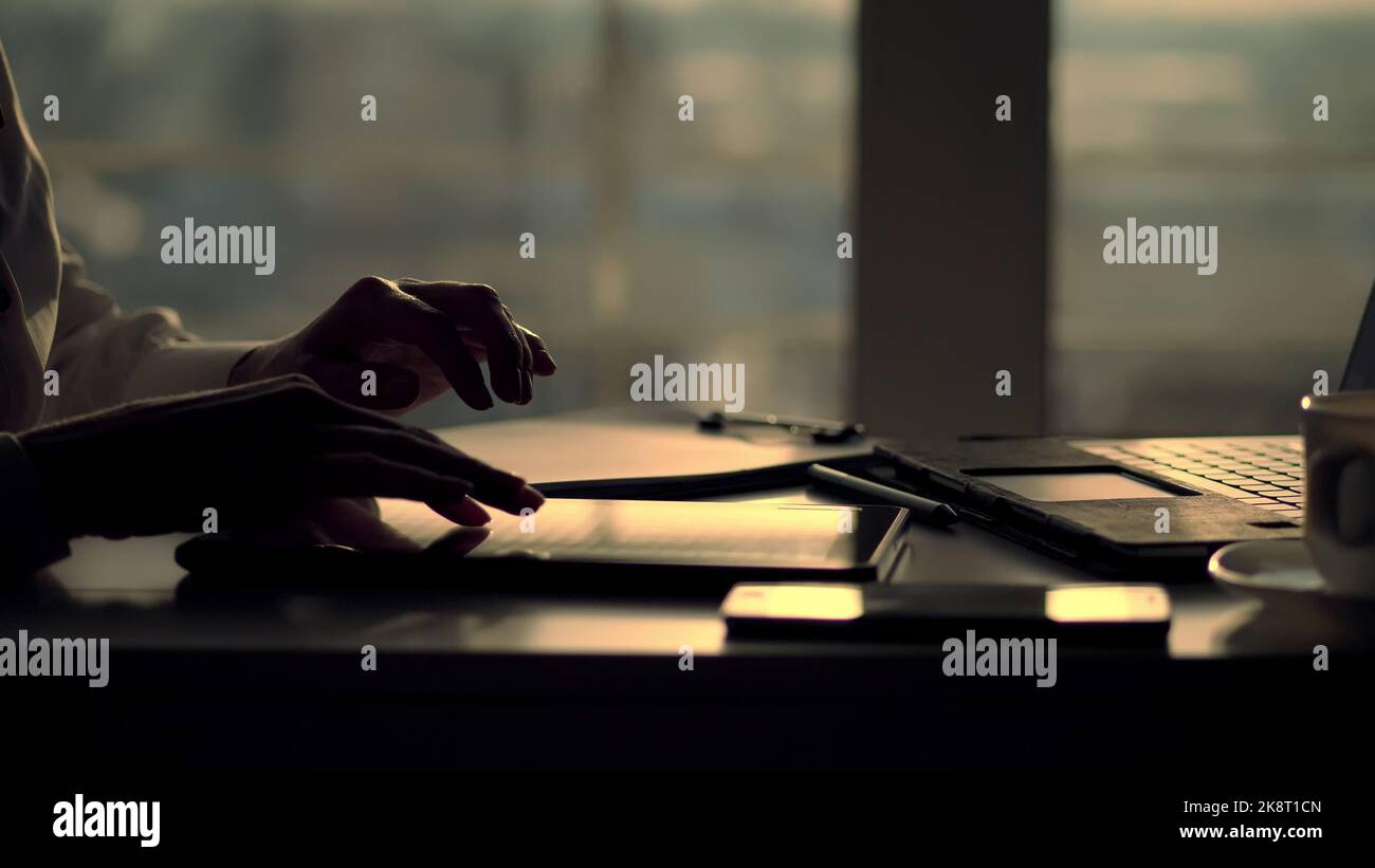 closeup, dark silhouette of female hands. she is typing something in ...