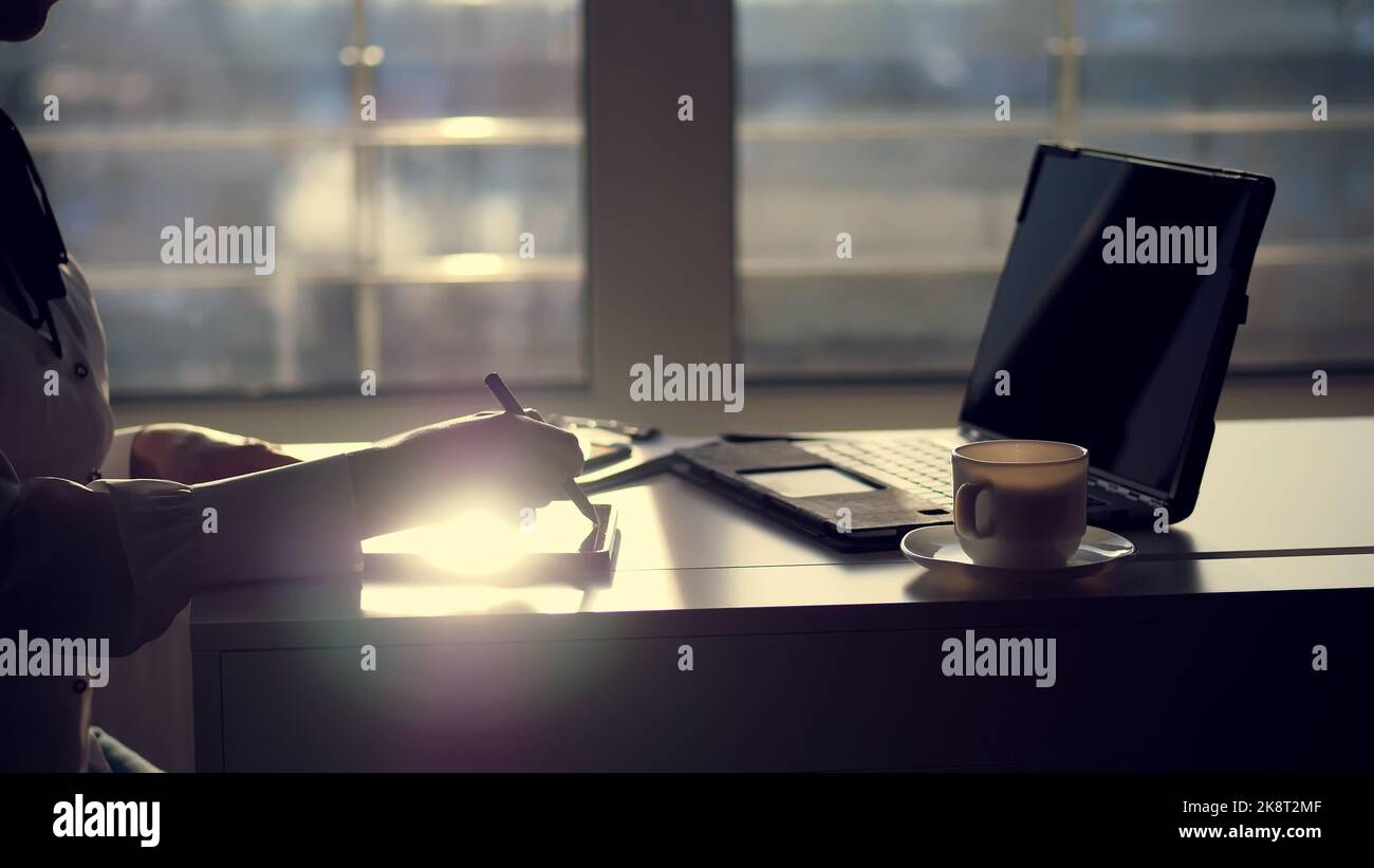 dark silhouette of businesswoman, closeup of hands. she writes ...