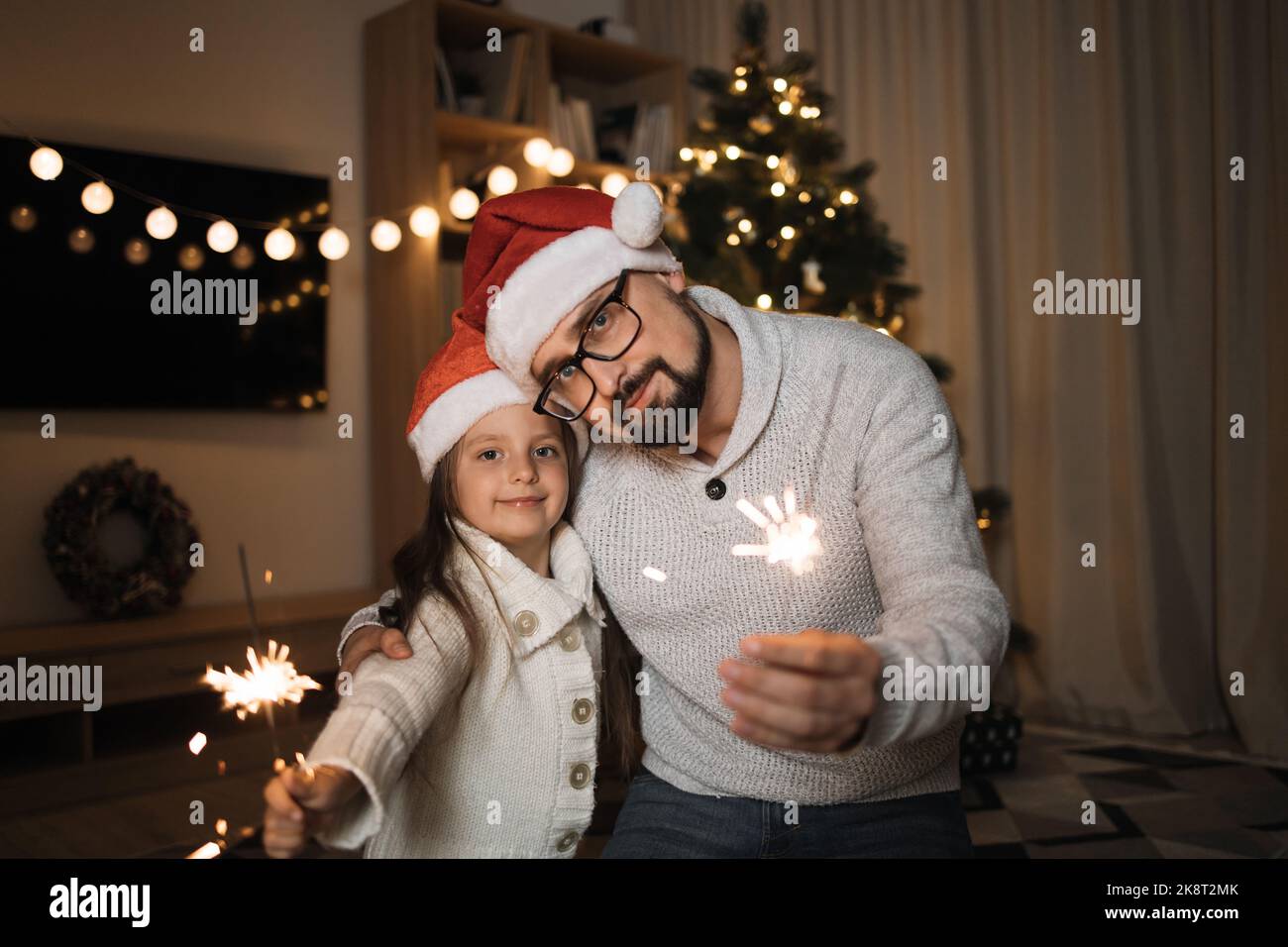 Smiling dad and little daughter in red santa hats, burning a sparkler ...