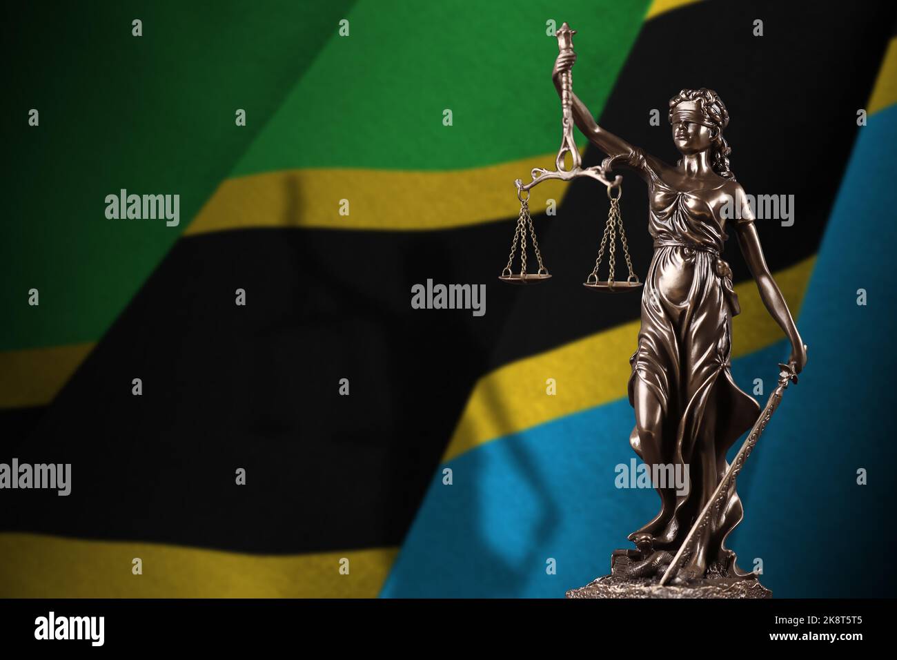 Tanzania flag with statue of lady justice and judicial scales in dark ...