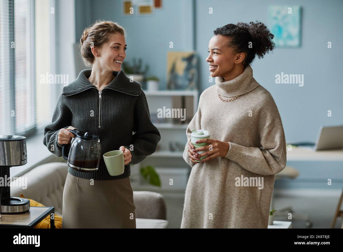 Two young colleagues drinking coffee together during break at office ...