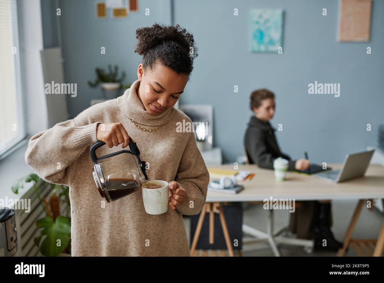 African young businesswoman pouring coffee into cup from teapot during break at office Stock ...