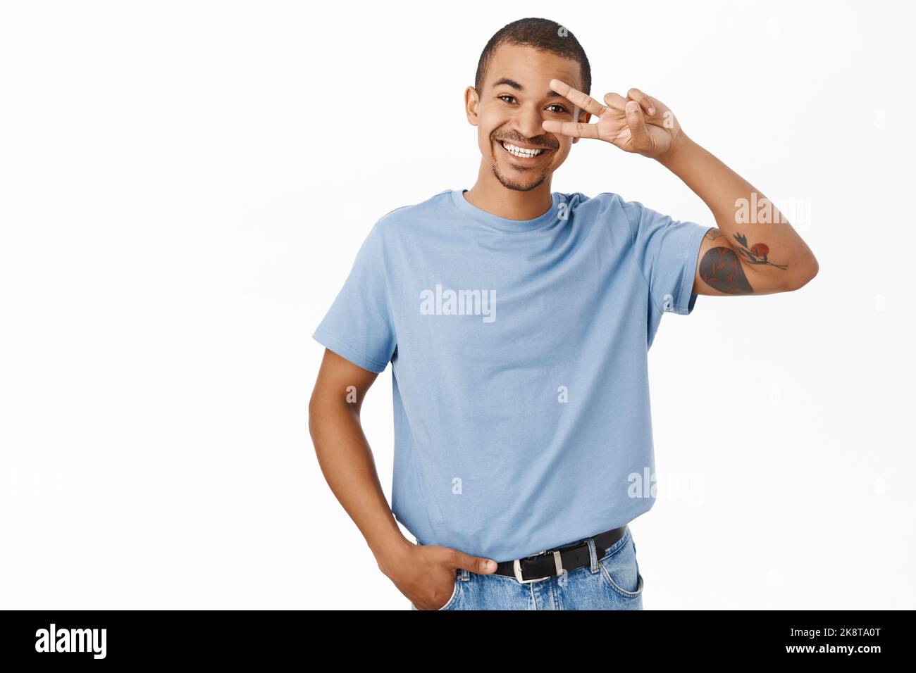 Positive guy shows peace, v-sign gesture and smiles, stands in casual ...