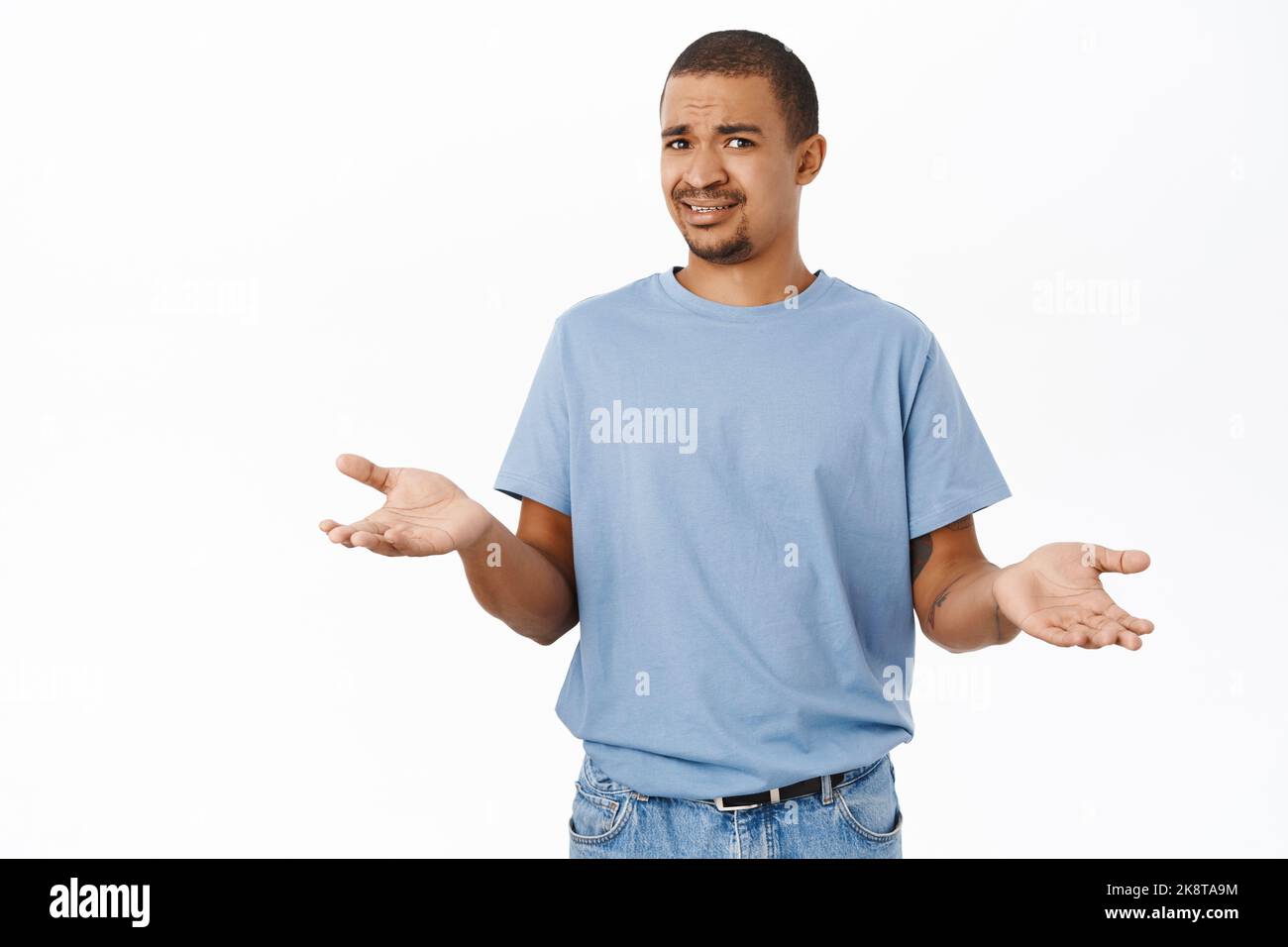 Portrait of young man shrugs and looks with confused face at camera ...