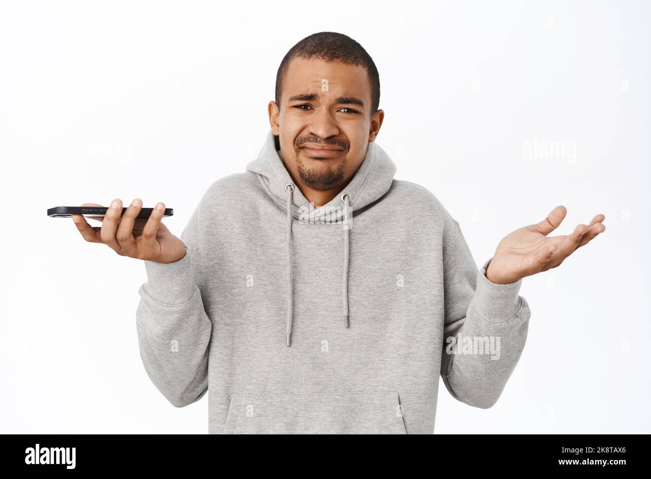 Man holds phone and shrugs shoulders, looks sad and confused, stands ...