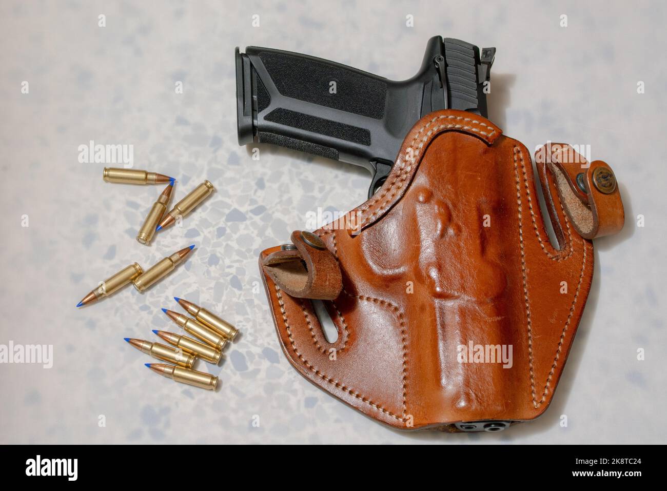 Picture of a firearm in brown holster next to bullets on a white ...