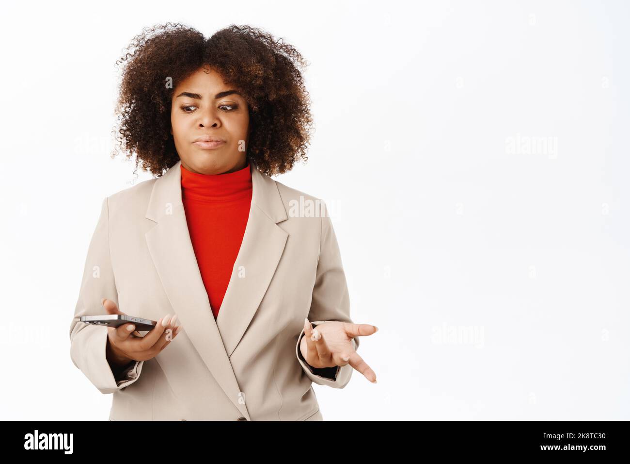 Businesswoman standing confused with smartphone in hand, standing over ...