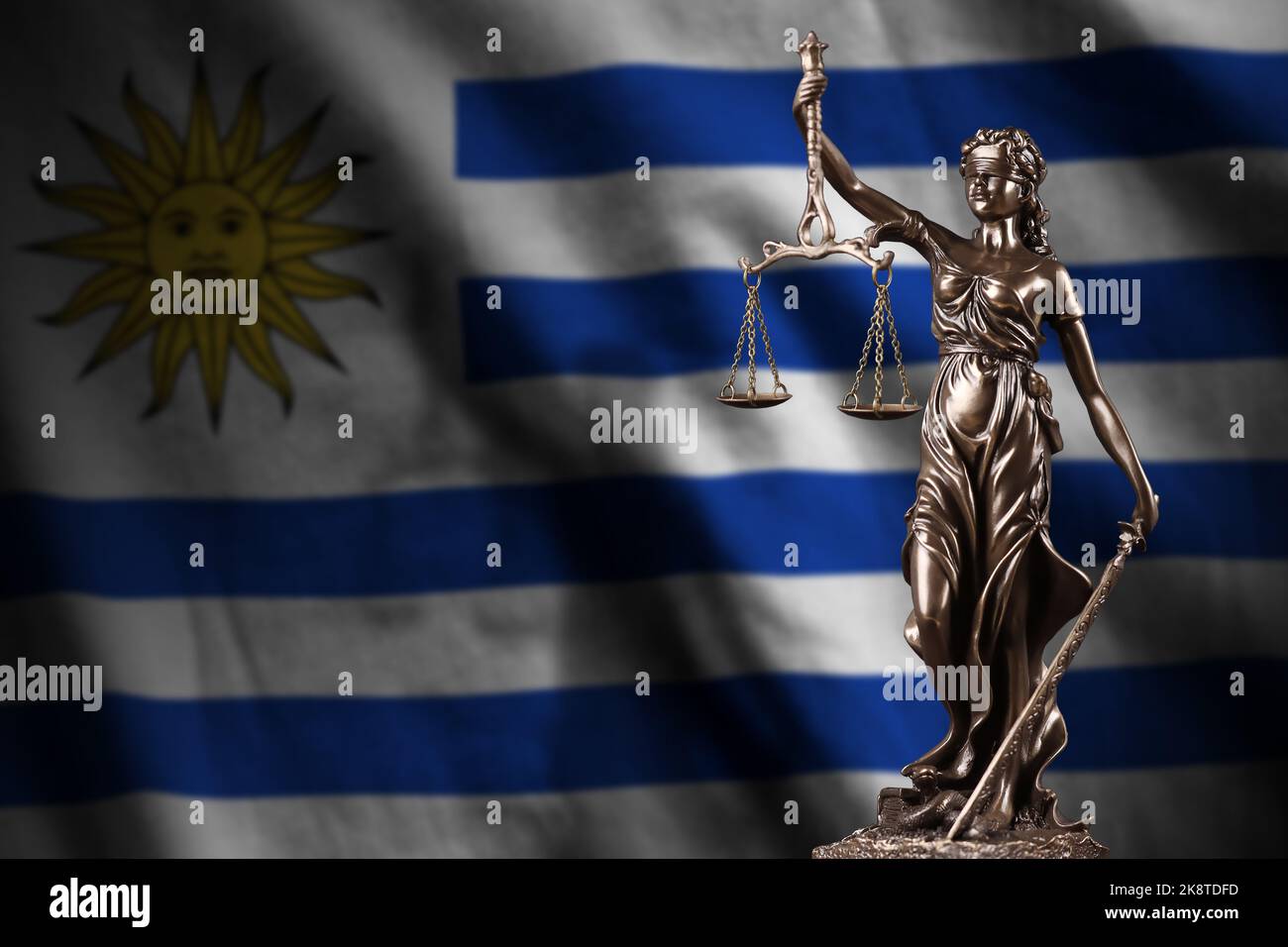 Uruguay flag with statue of lady justice and judicial scales in dark ...