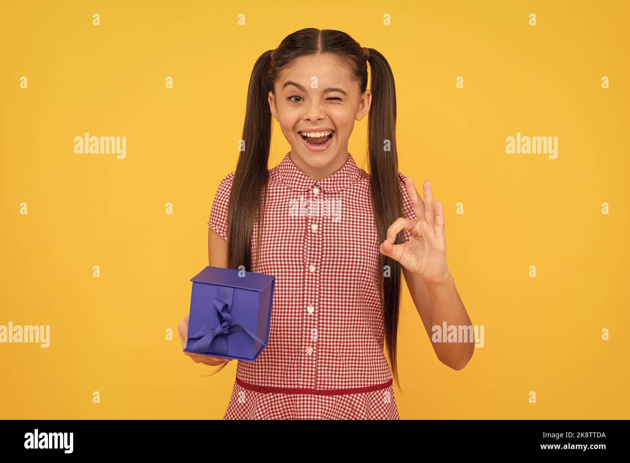 happy kid hold present box on yellow background winking with ok gesture ...