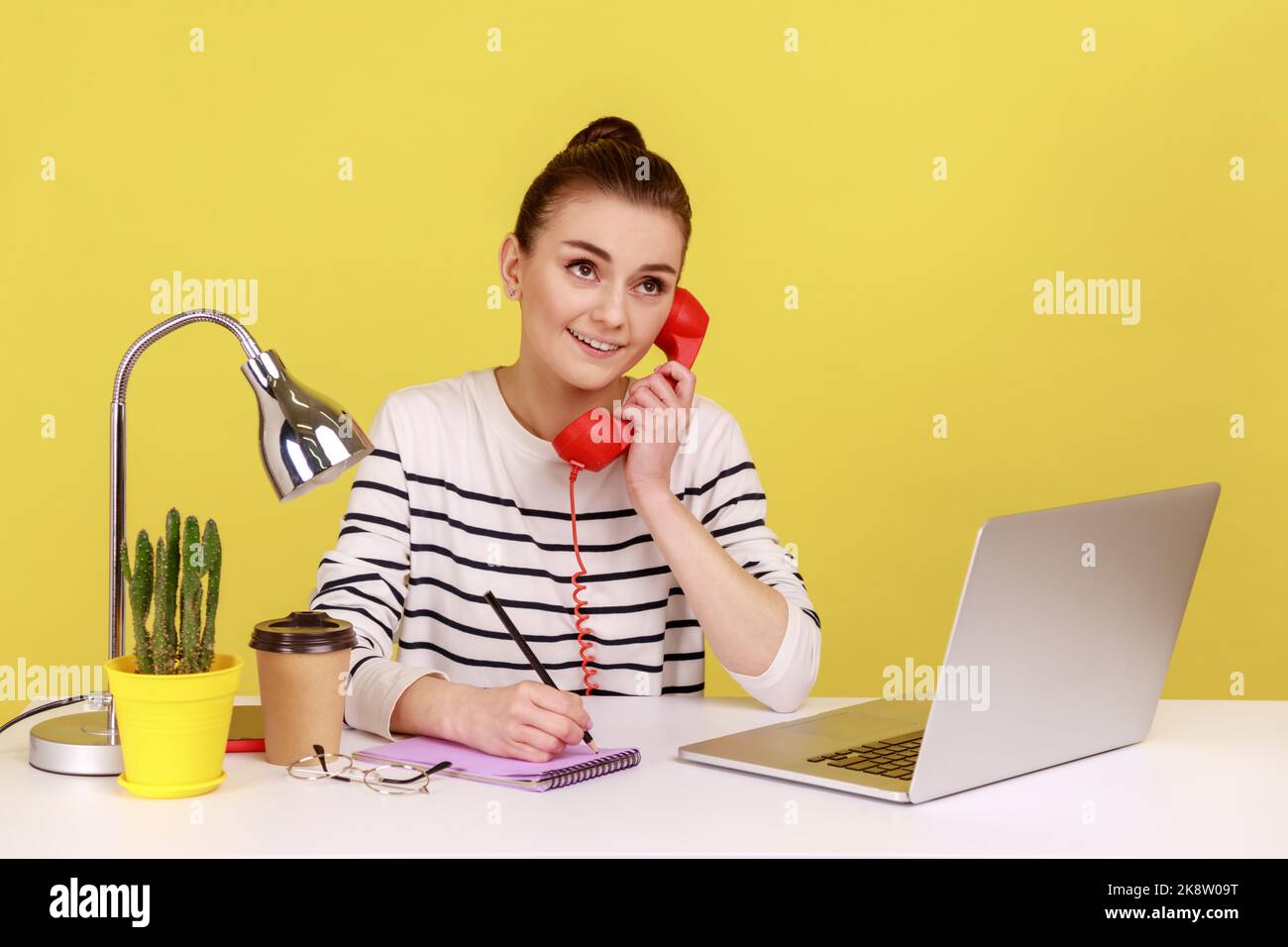 Portrait of smiling woman talking on red retro phone, looking away with ...