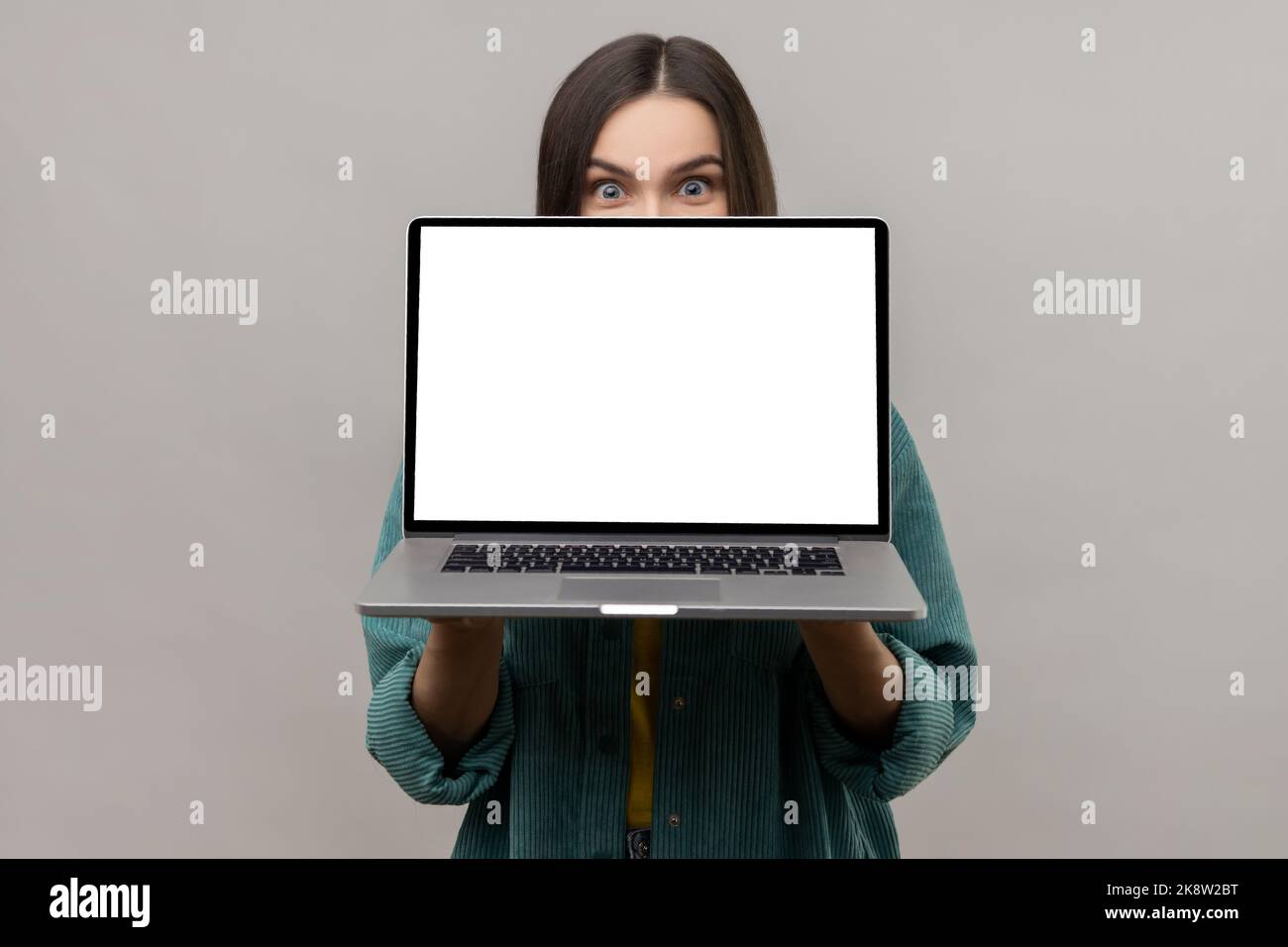 Positive unknown woman hiding half of face behind laptop with white ...