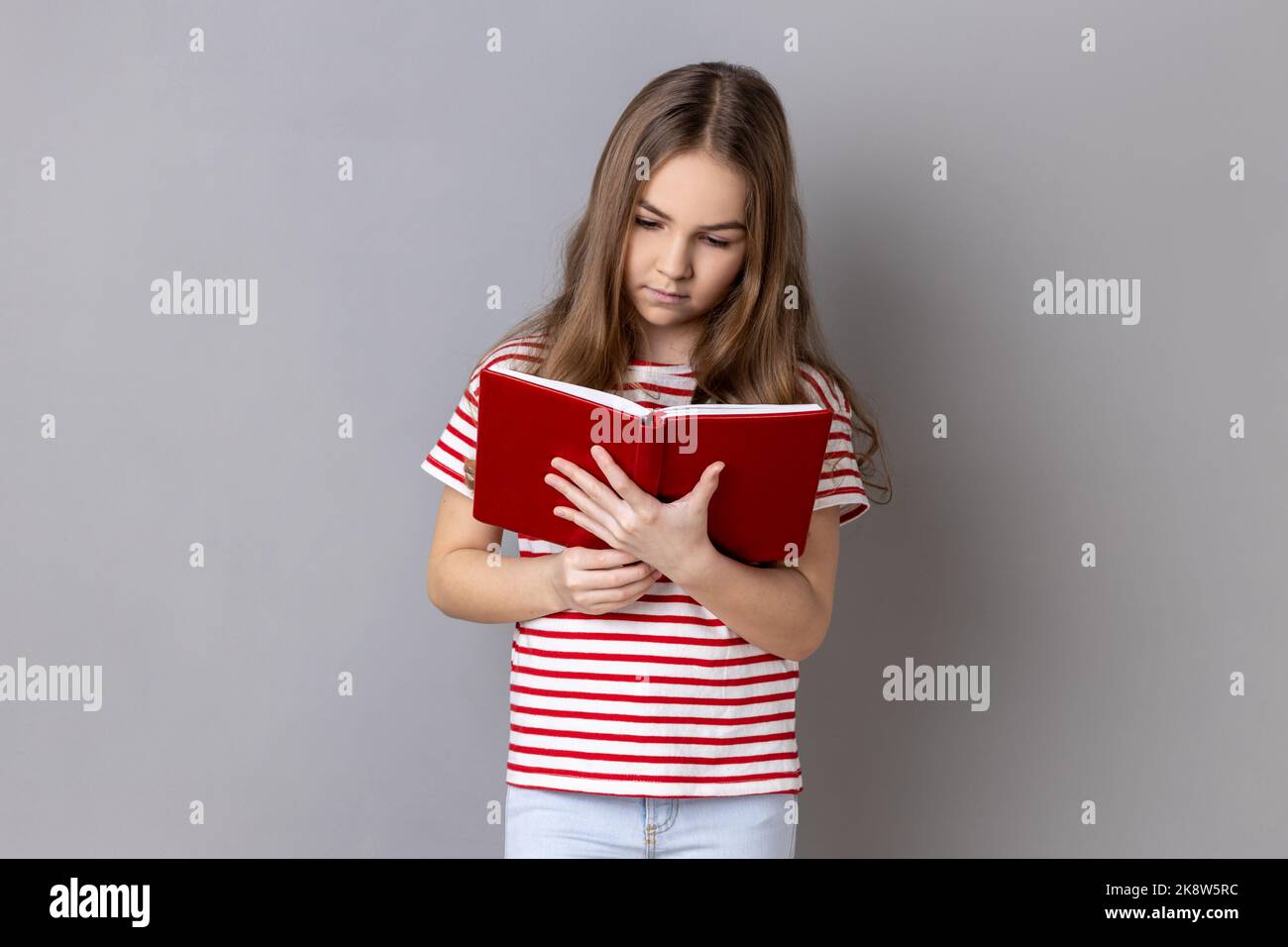 Portrait of concentrated dark haired little girl wearing striped T ...
