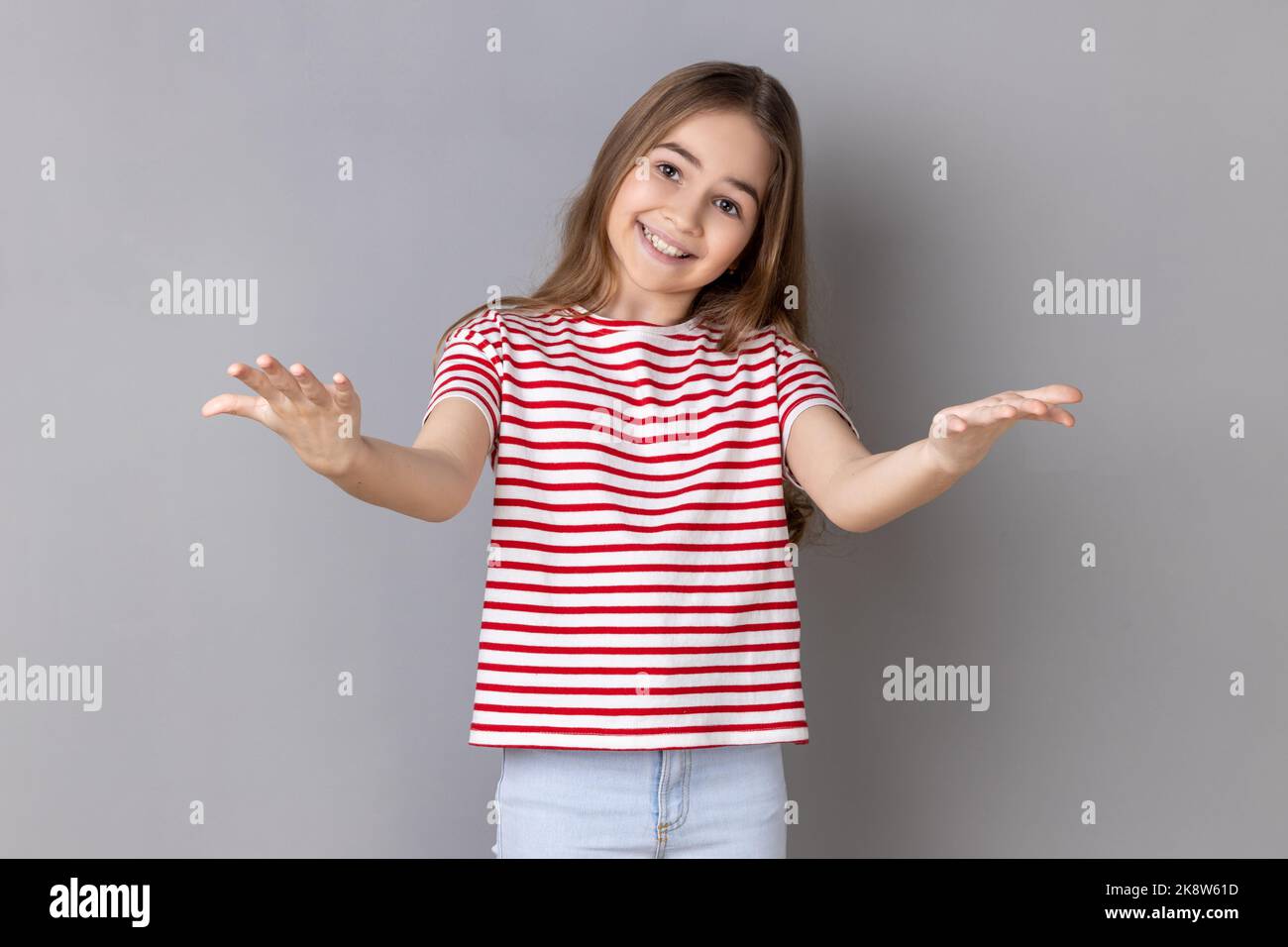 Portrait of little girl wearing striped T-shirt outstretching hands ...