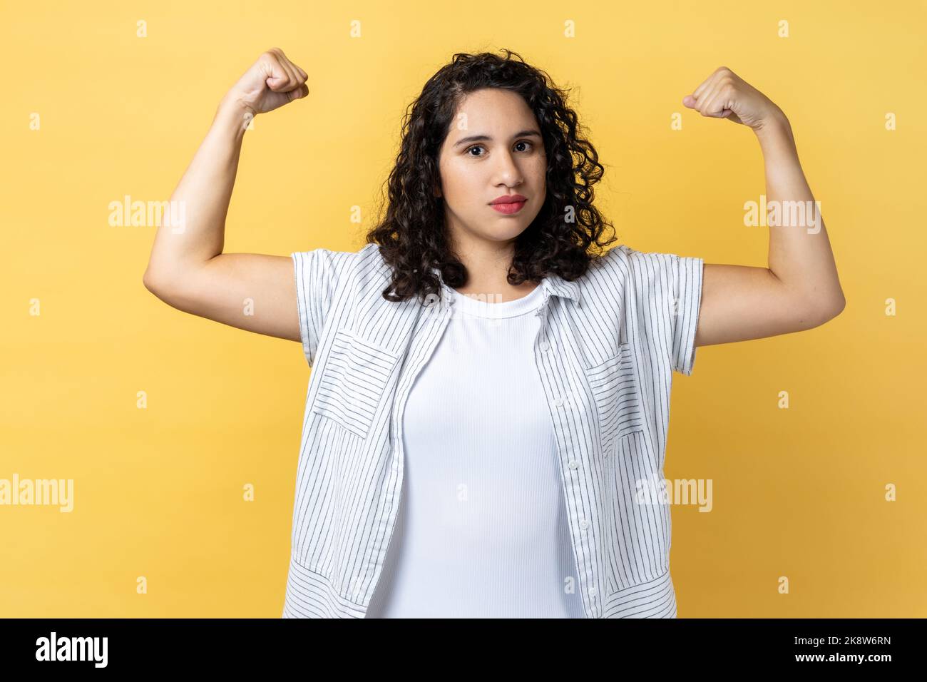 Yes, I am winner. Portrait of woman with dark wavy hair raises arms ...