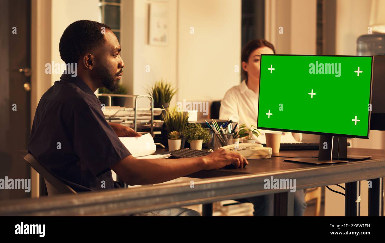 Male Manager Looking At Computer With Greenscreen Display Working With