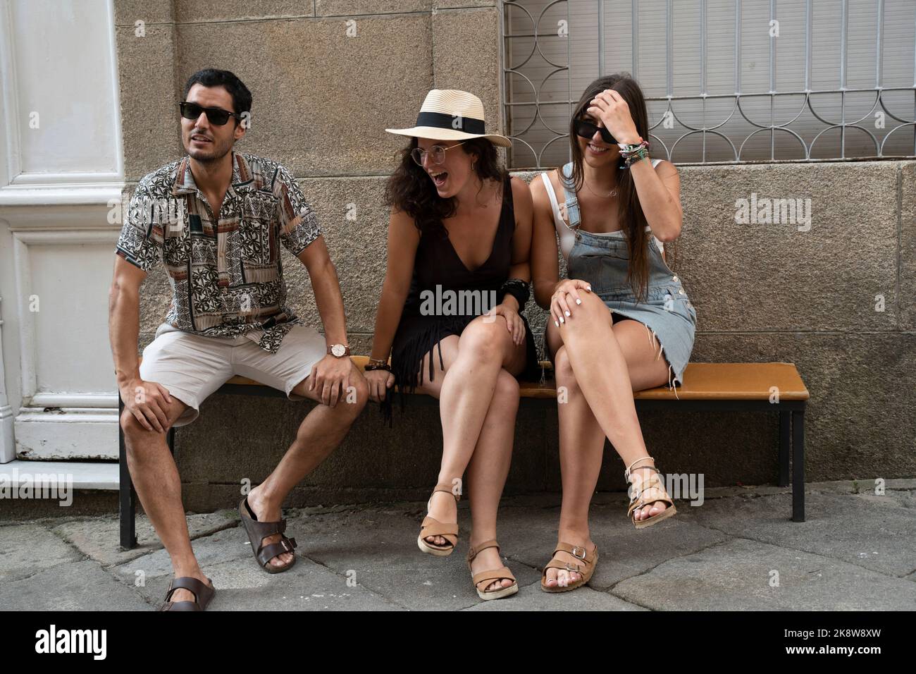 a group of three friends having fun and laughing on a bench in the ...