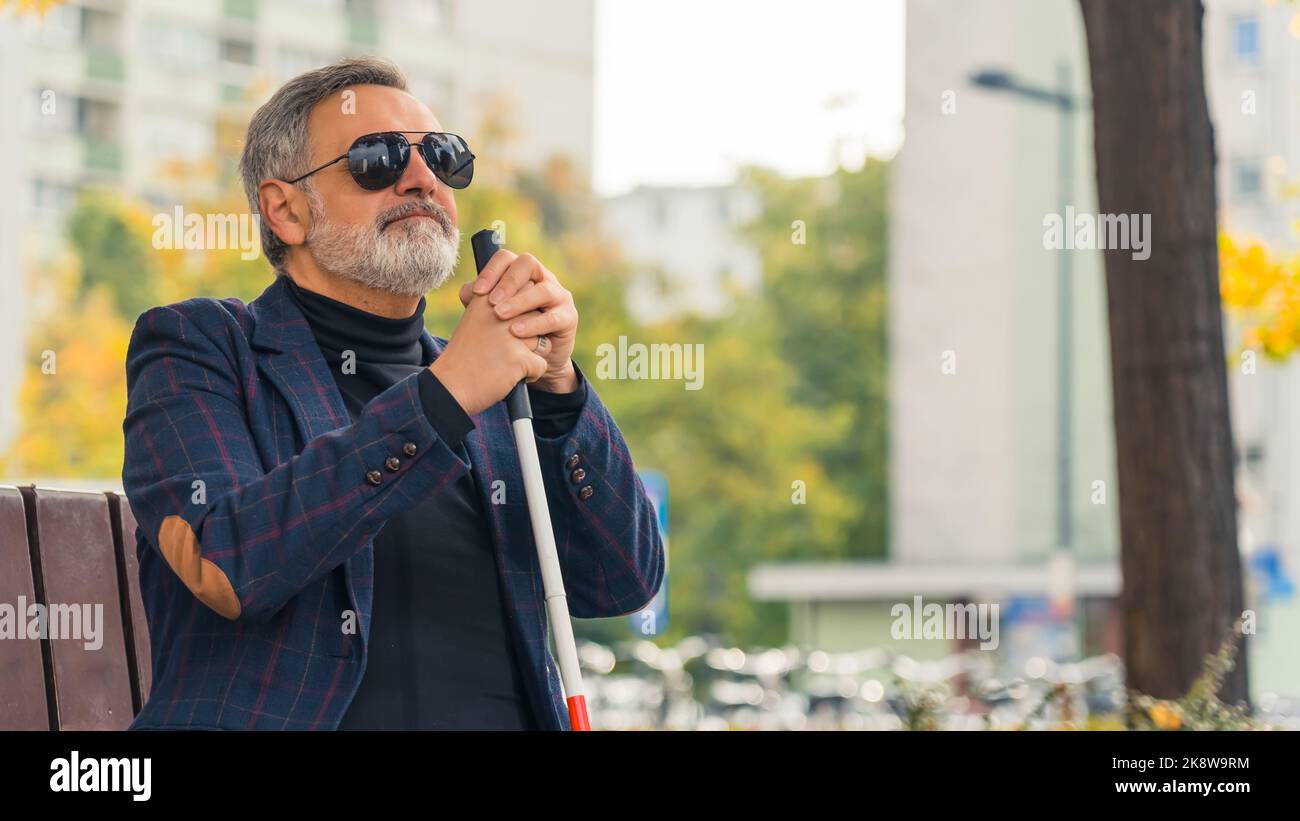 Middle-aged grey-haired blind man in sunglasses resting on bench ...