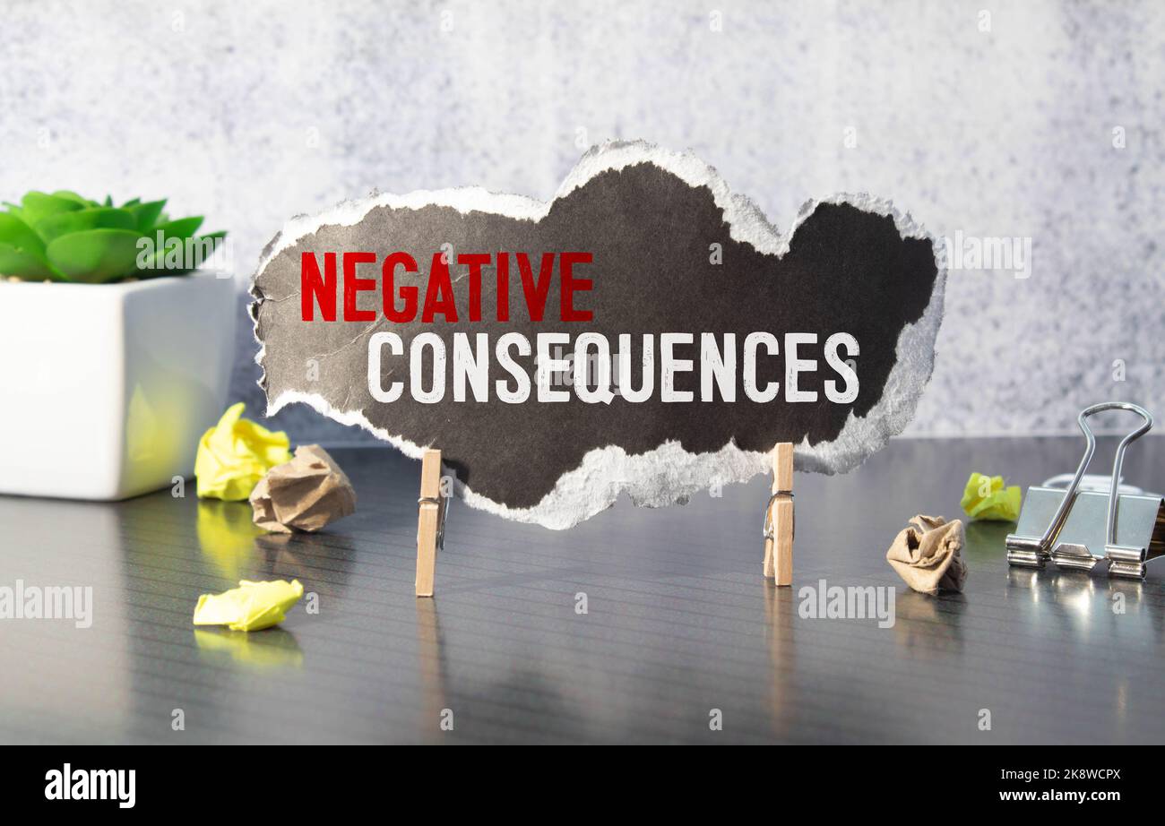 Closeup on businessman holding a card with text NEGATIVE CONSEQUENCES ...