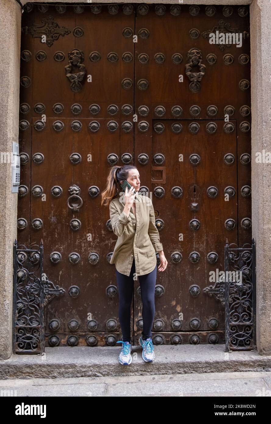 Young female in the city in front door of the house talking on her ...