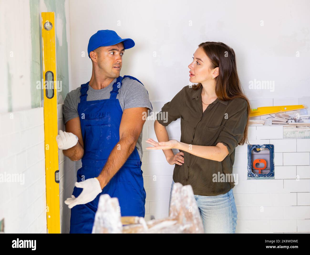 Worker using spirit level on wall with woman client Stock Photo - Alamy